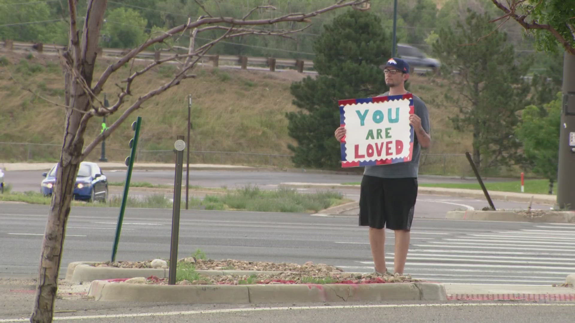 Man stands at intersection holding sign in memory of his late sister ...